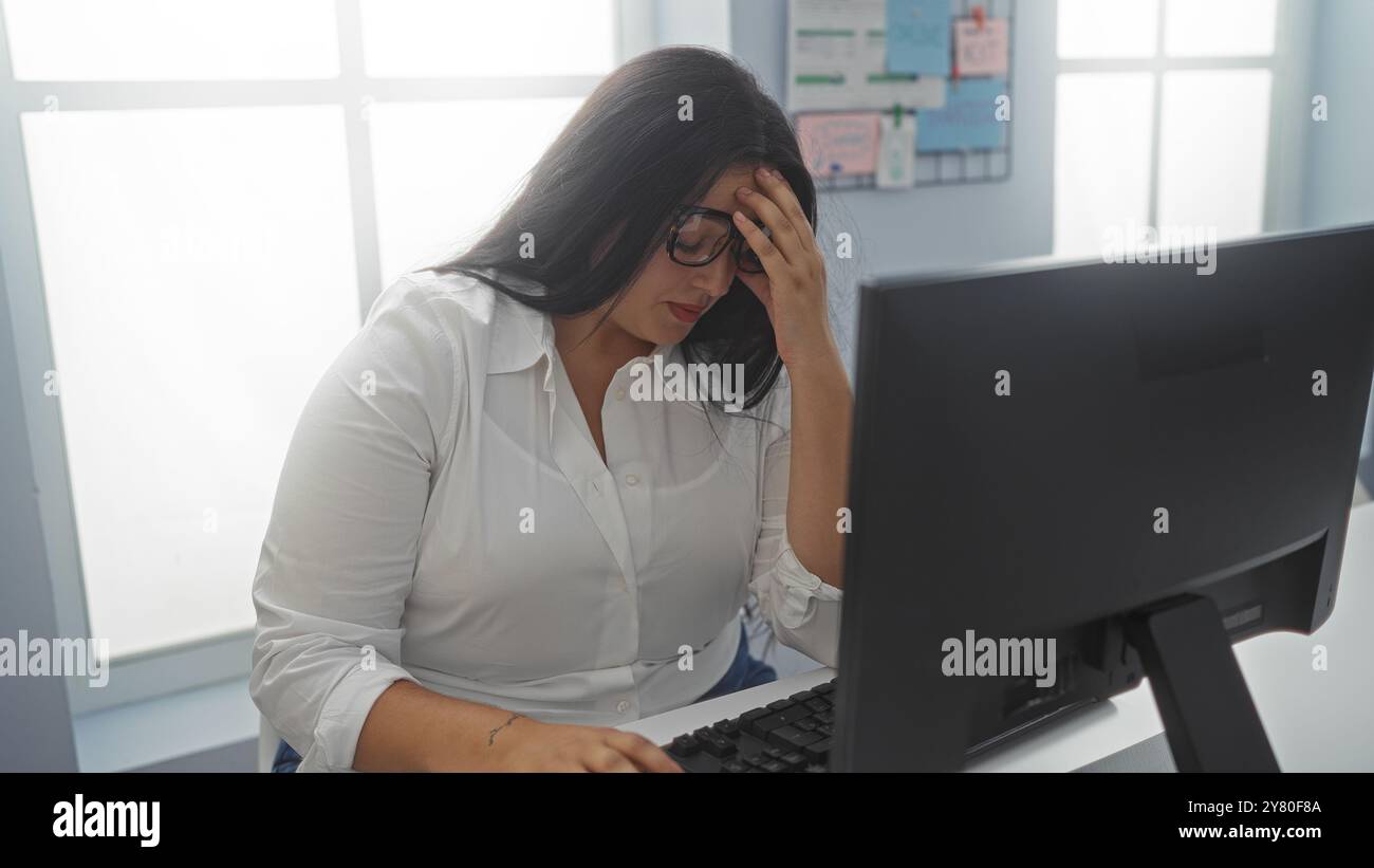 Plus size woman wearing glasses stressed at her computer workstation in an office Stock Photo ...