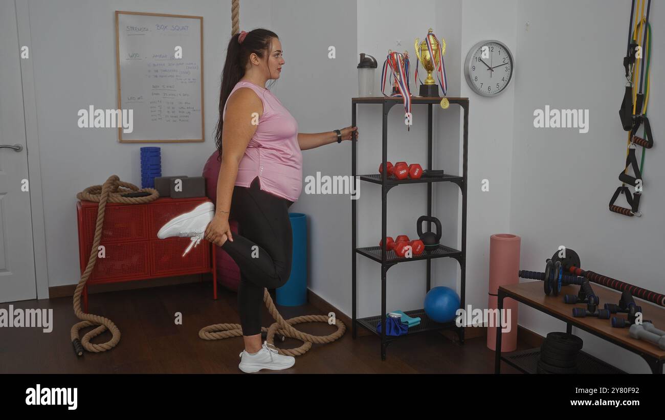Woman stretching indoors at gymnasium with fitness equipment and wall ...