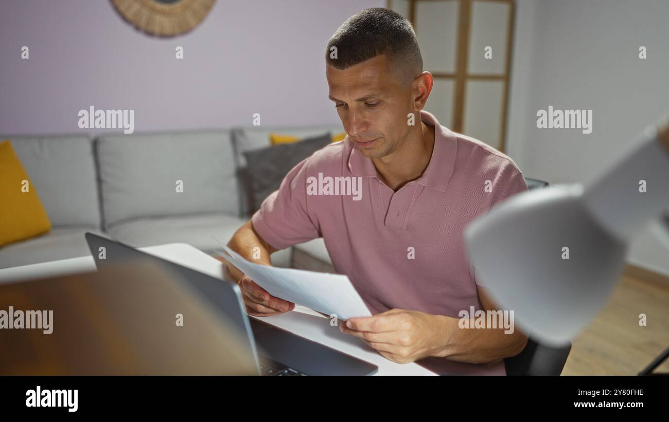 Young man sitting in a living room holding documents while working on a ...