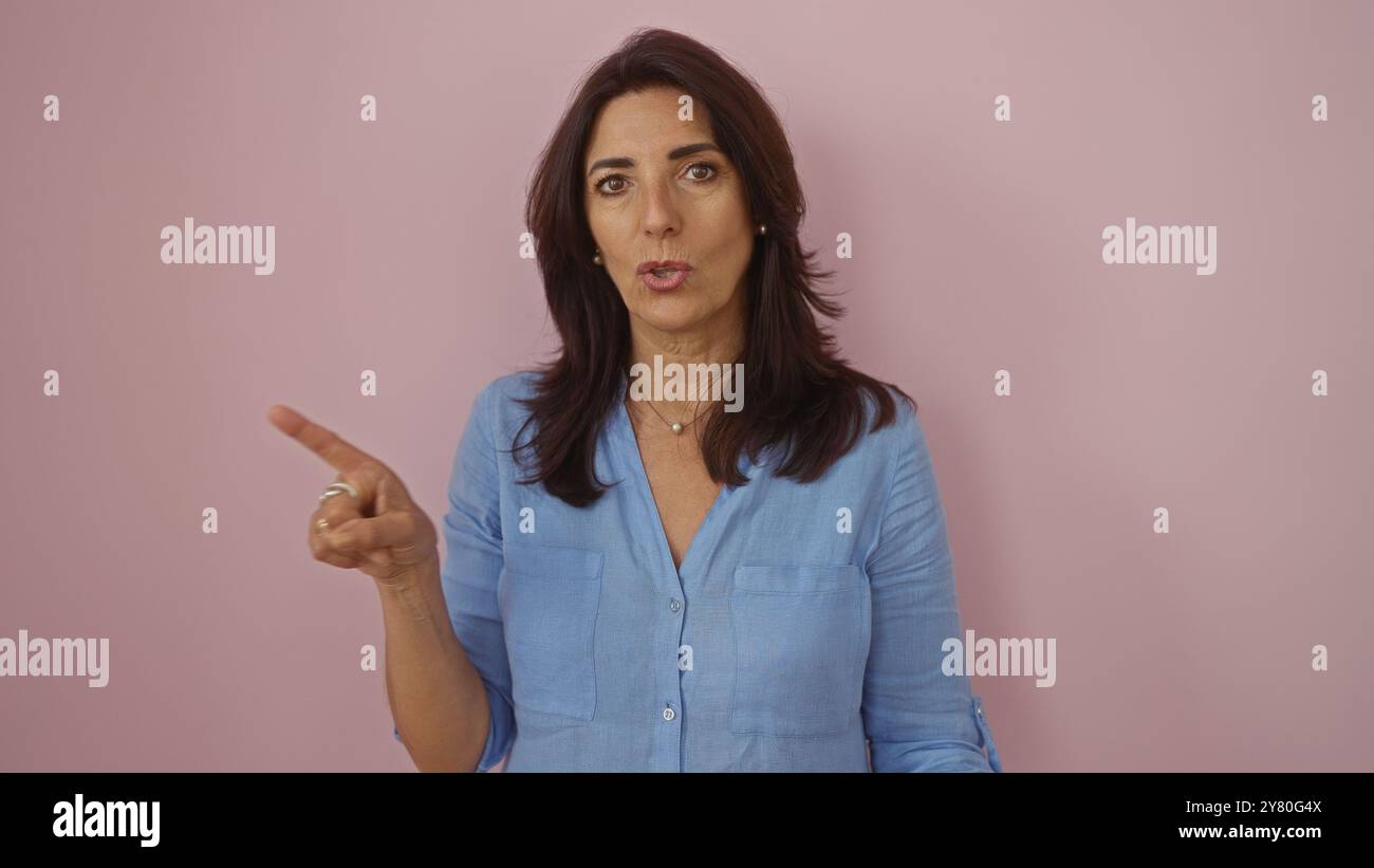Woman pointing upward in front of an isolated pink background, wearing ...