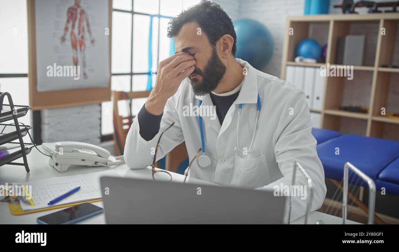 Stressed man in white lab coat at a clinic desk with anatomical poster ...
