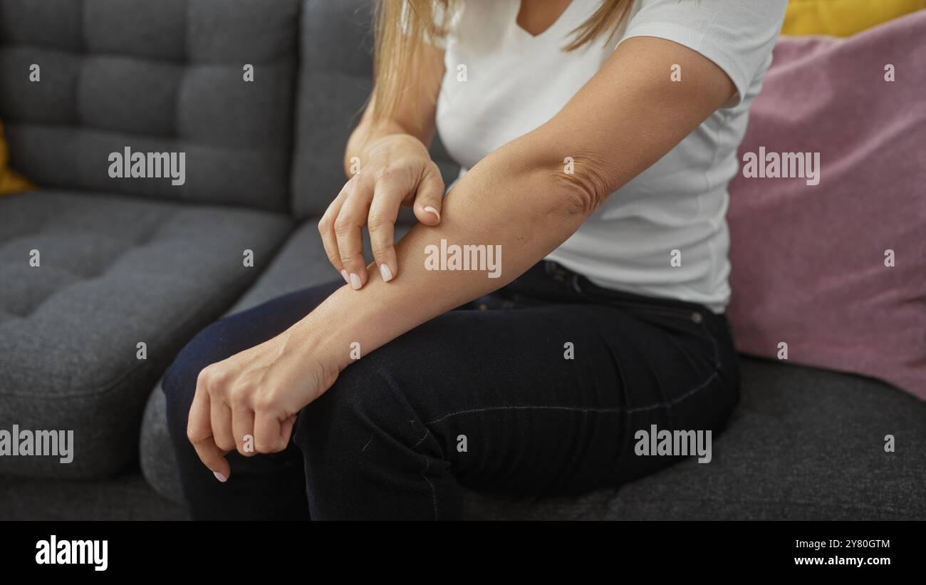 A woman scratches her arm while sitting on a modern grey sofa in a cozy ...