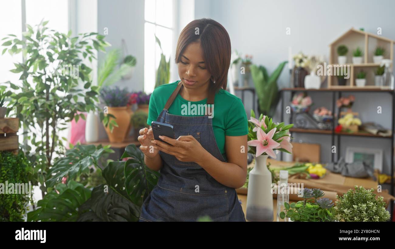 A focused african american woman florist using a smartphone in a flower ...