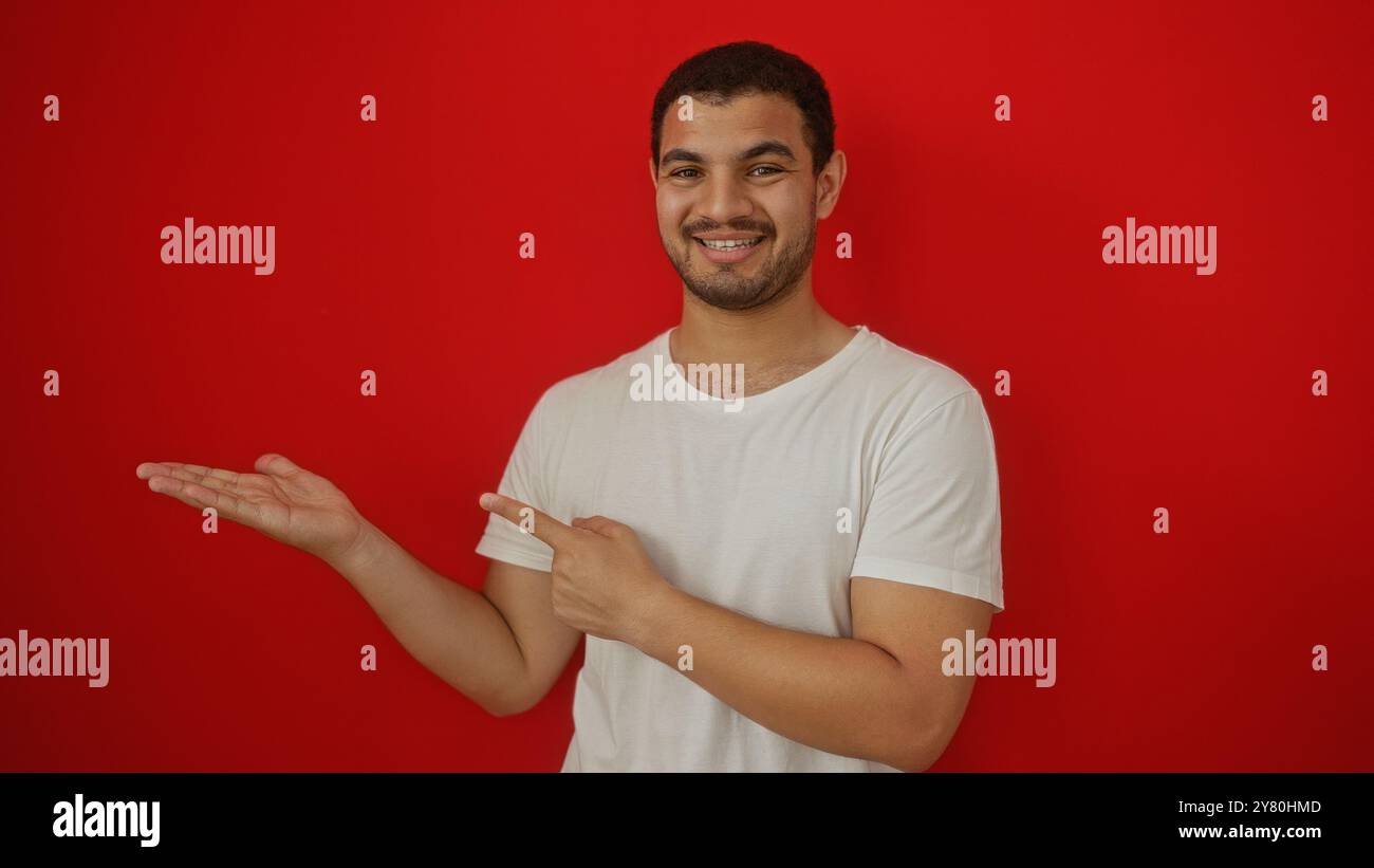 Young man in white shirt pointing to open palm against red background ...