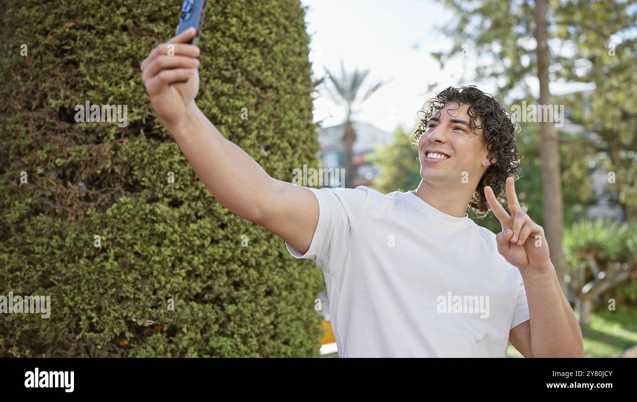 A happy young man with curly hair takes a selfie outdoors with nature ...