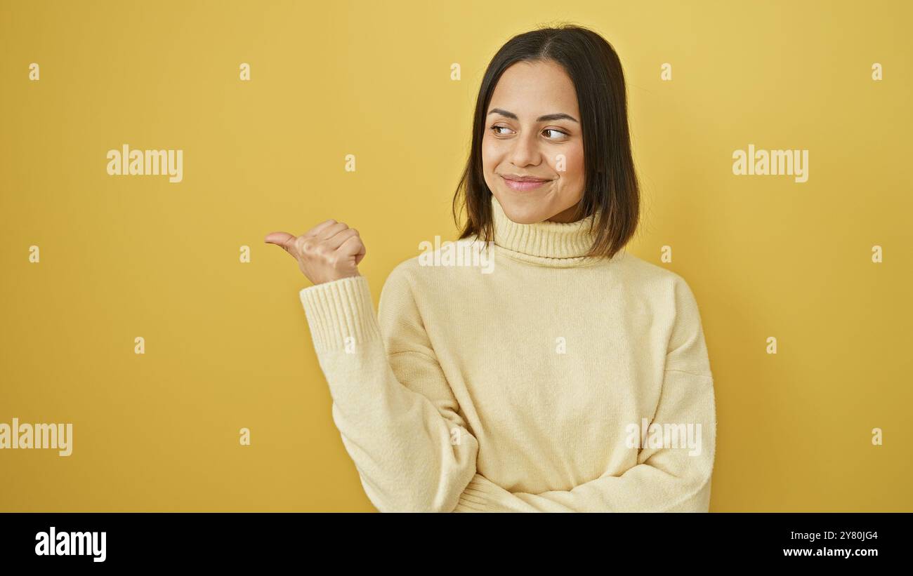 Hispanic young woman thumb pointing isolated on yellow background with ...