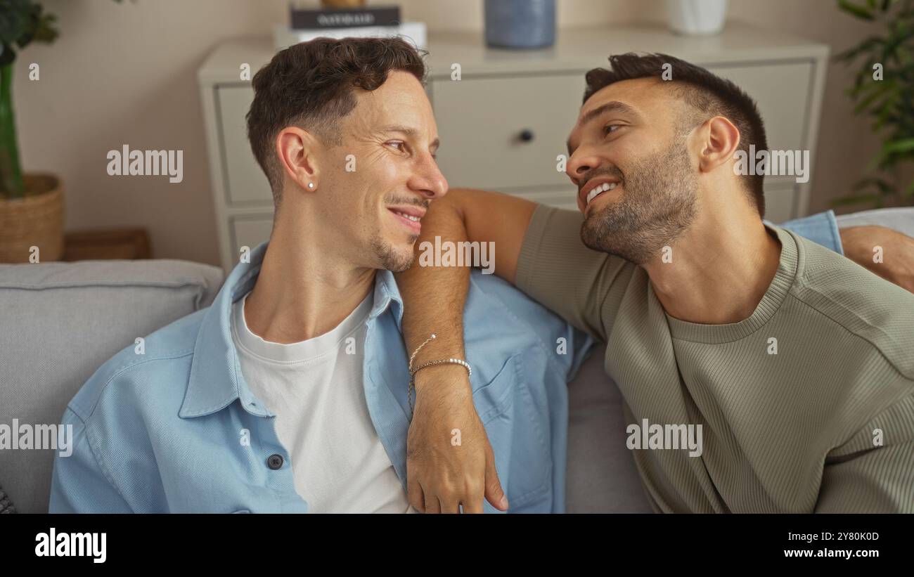 Two men sitting together in a cozy living room, smiling and gazing at ...