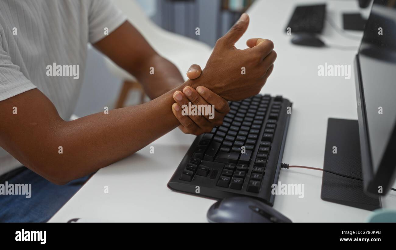Young man in an office holding his wrist in pain, sitting at a desk ...