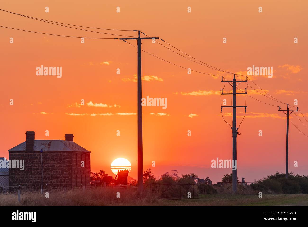 A colourful sunset behind a homestead building and a line of power ...