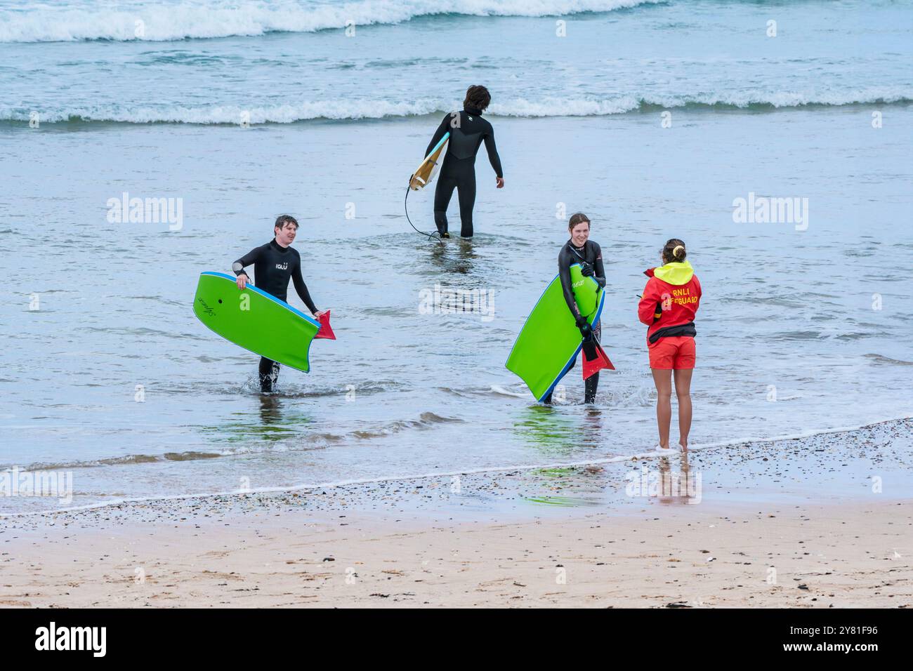 Bodyboarders talking to a female RNLI Lifeguard on Fistral beach in ...