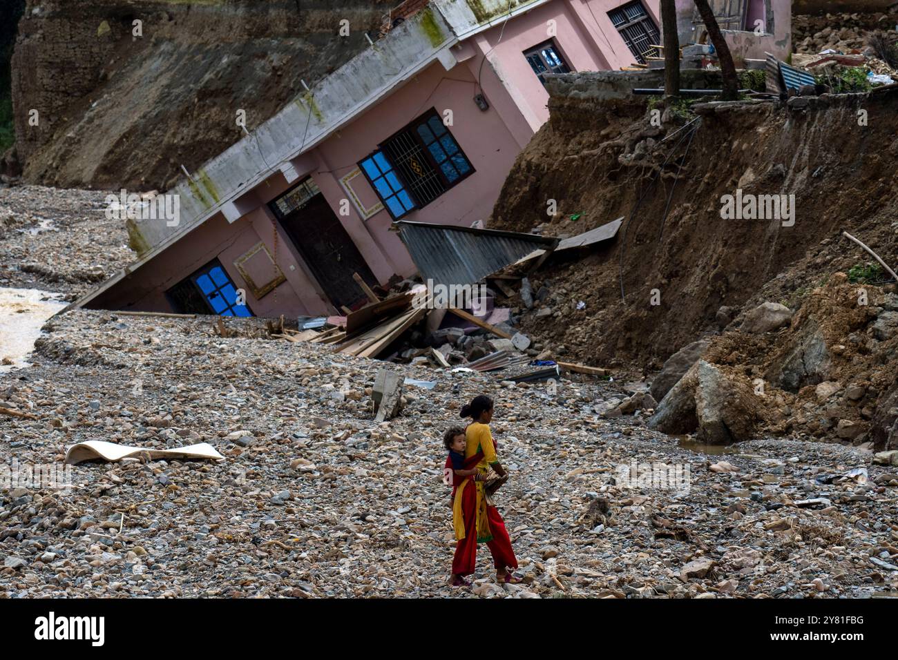 A woman with a child on her back walks past a house which had collapsed ...