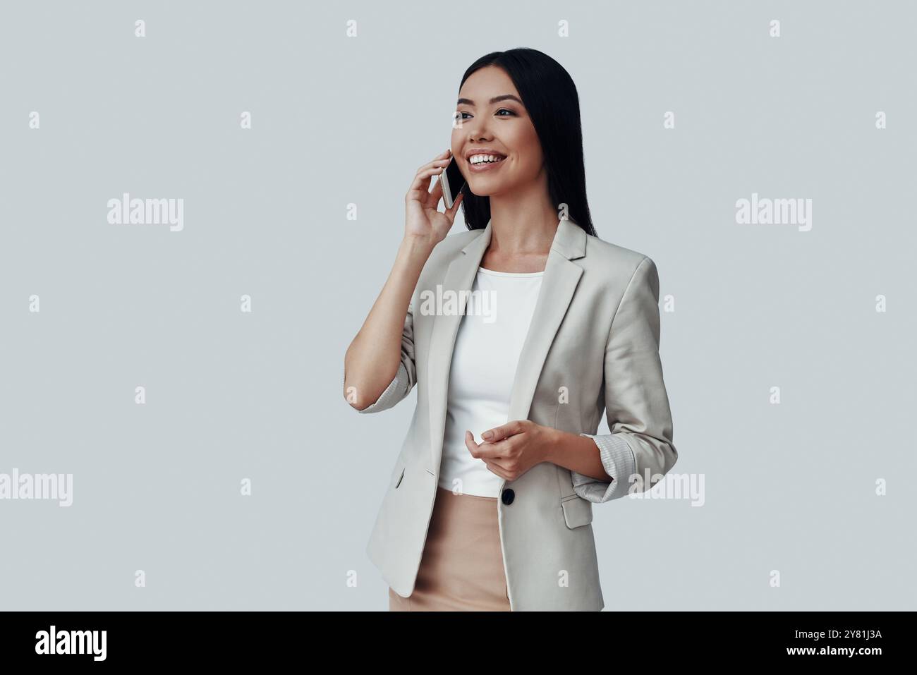 Good talk. Attractive young Asian woman talking on the phone and smiling while standing against ...