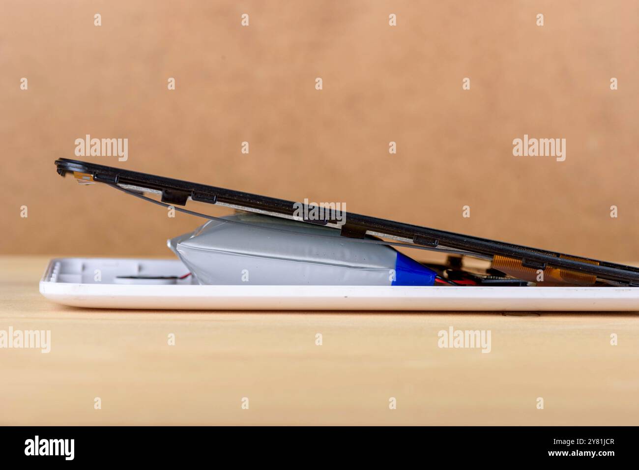 Disassembled smartphone with a swollen battery on a wooden surface ...