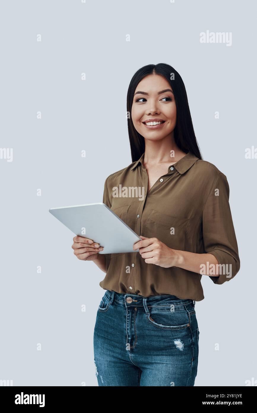 Modern technologies. Attractive young Asian woman looking away and smiling while standing ...