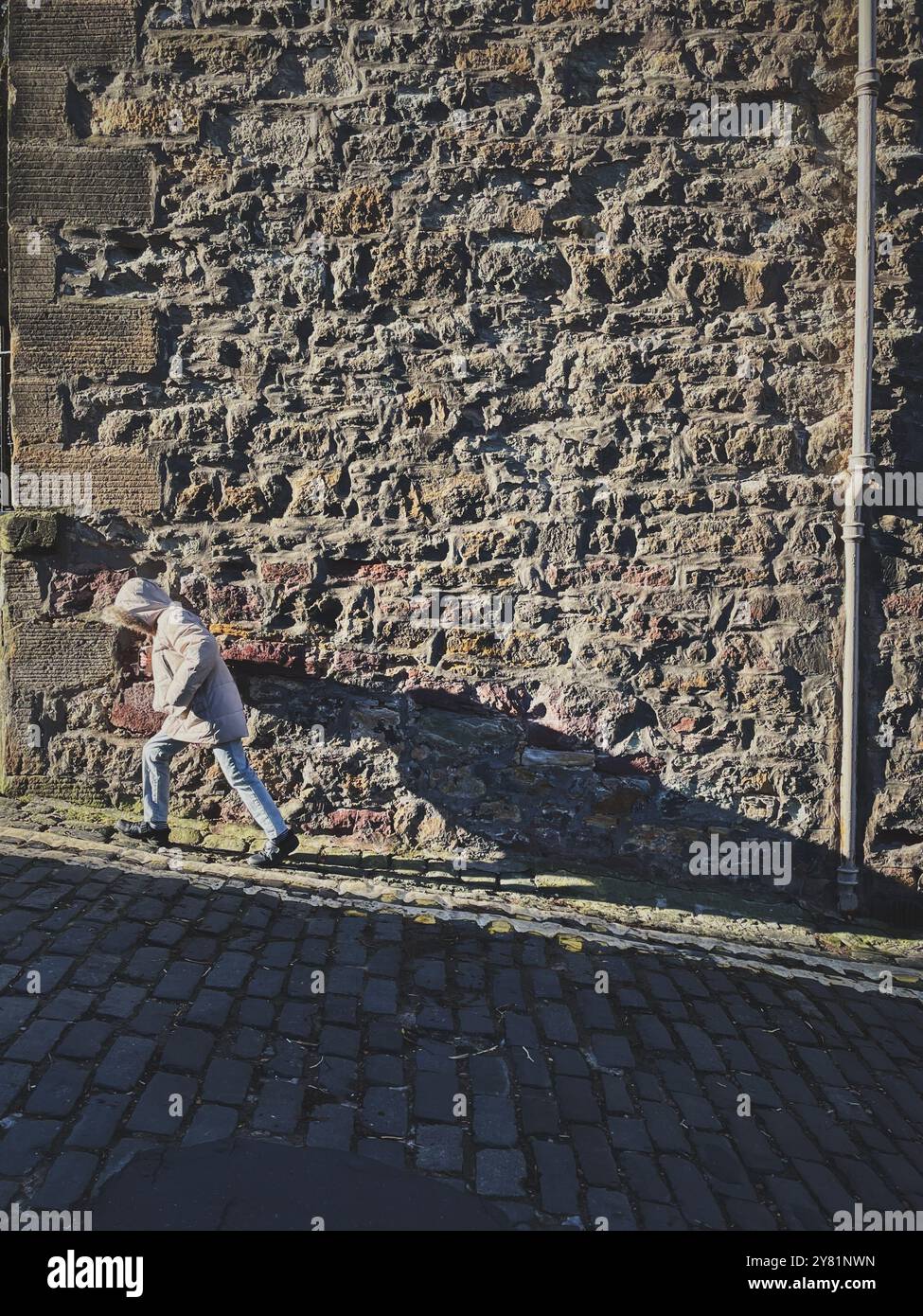 Boy with long shadow, walking up steep inclined road against building ...
