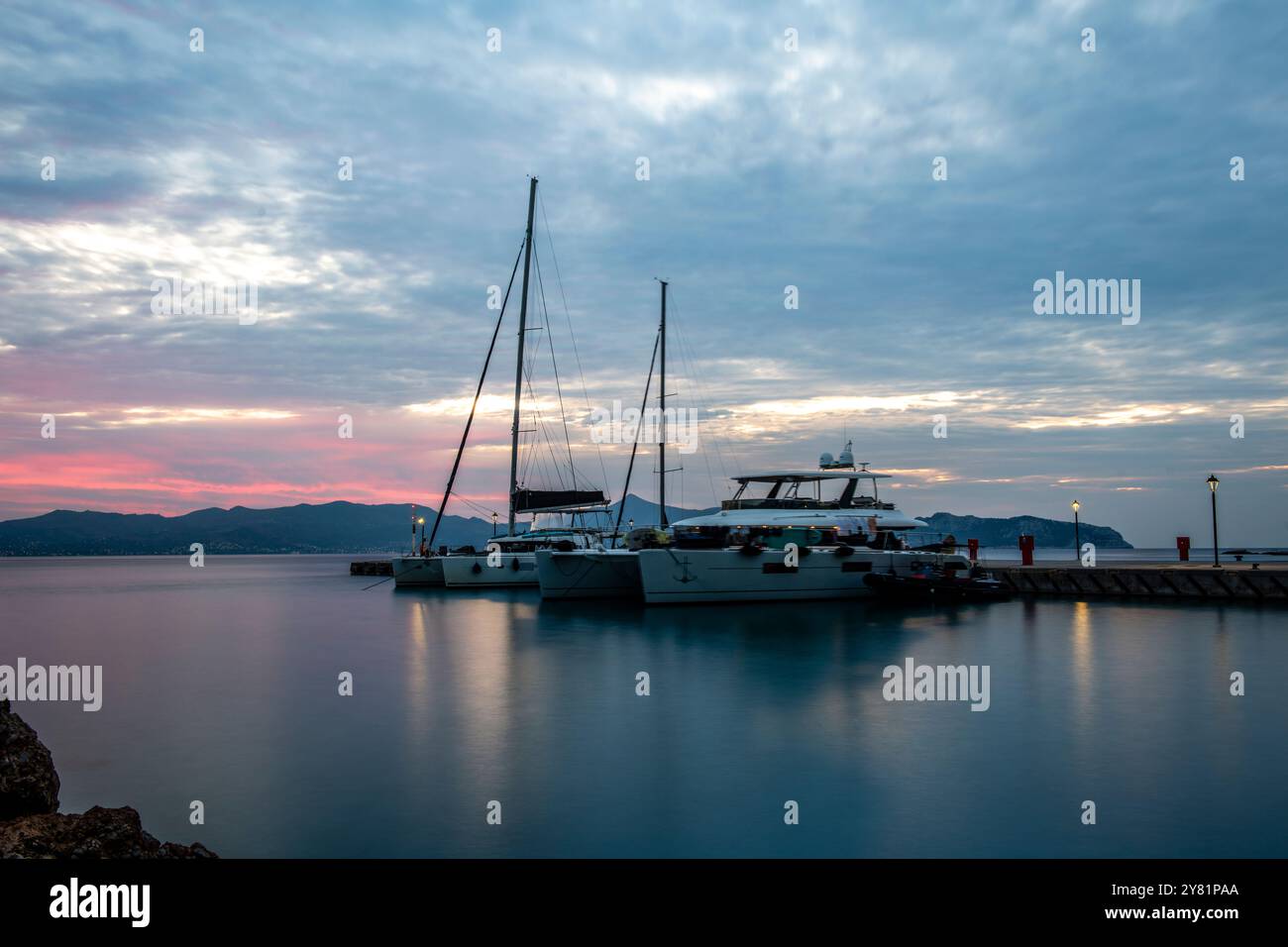 Luxury yachts moored overnight sit on calm still sea as day breaks over ...