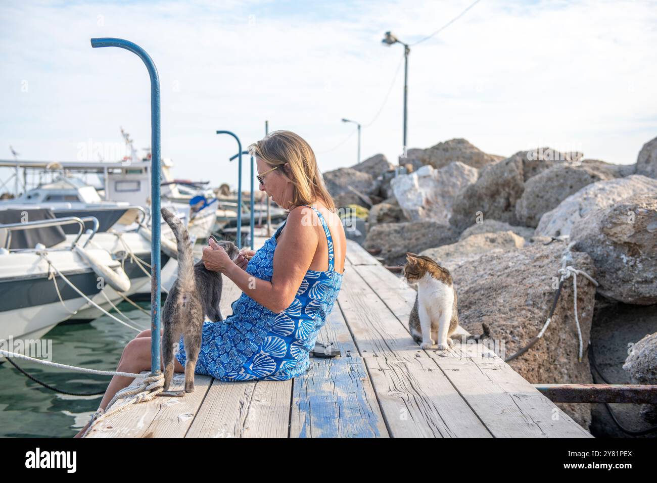 A kind lady feeds the wild cats on the side of the old port in Skala ...