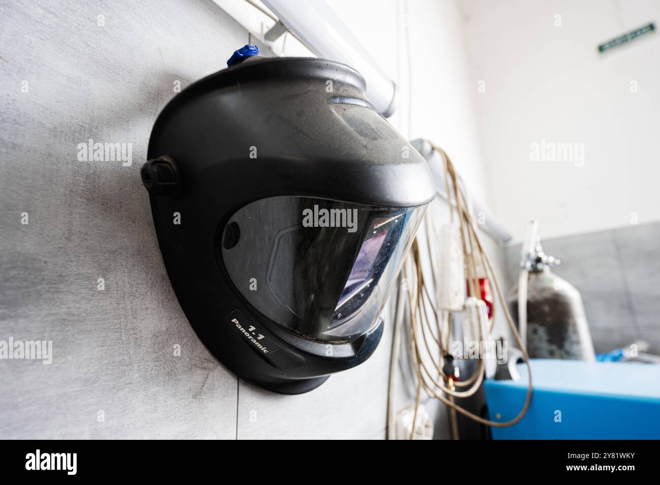 A black welding helmet hanging on the wall of an industrial workshop ...