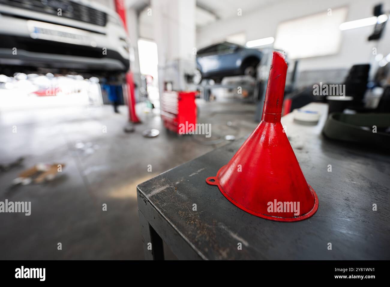 A red funnel placed on a workbench in a busy car repair garage, with ...