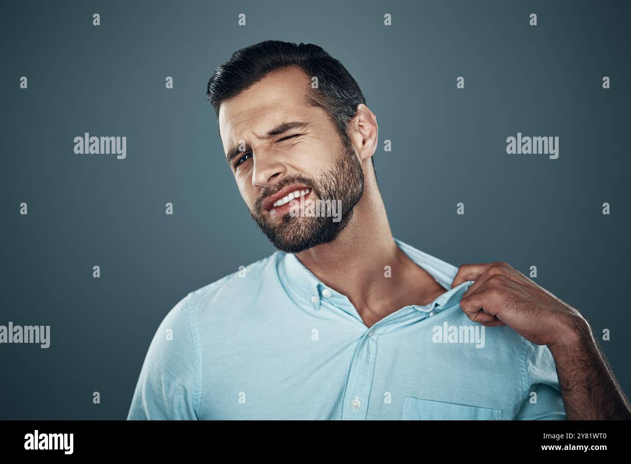 Uncomfortable. Tired young man pulling collar while standing against ...