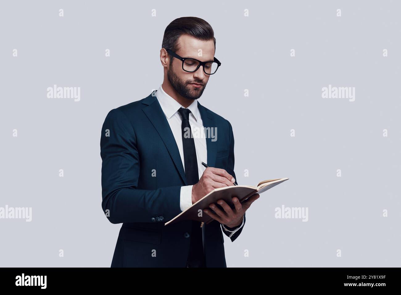 Making notes. Handsome young man writing something down while standing ...