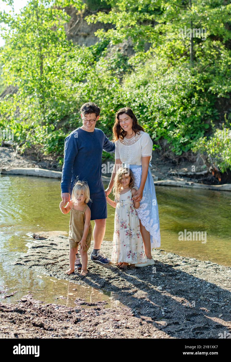 A family of four stands smiling on a sandy riverbank, with two adults ...