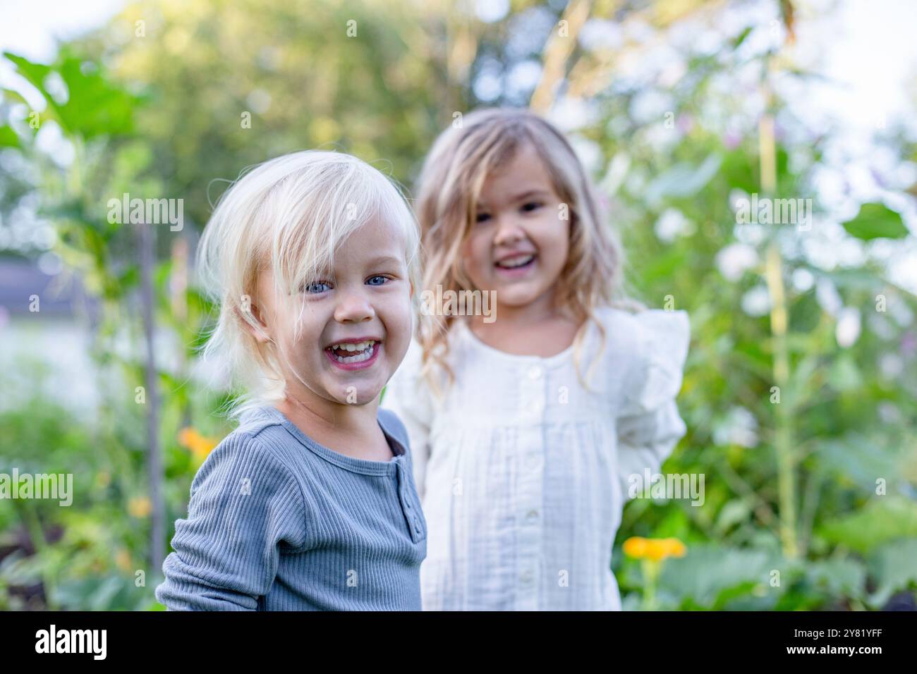 Two young children smiling in a garden, with one having blond hair and ...