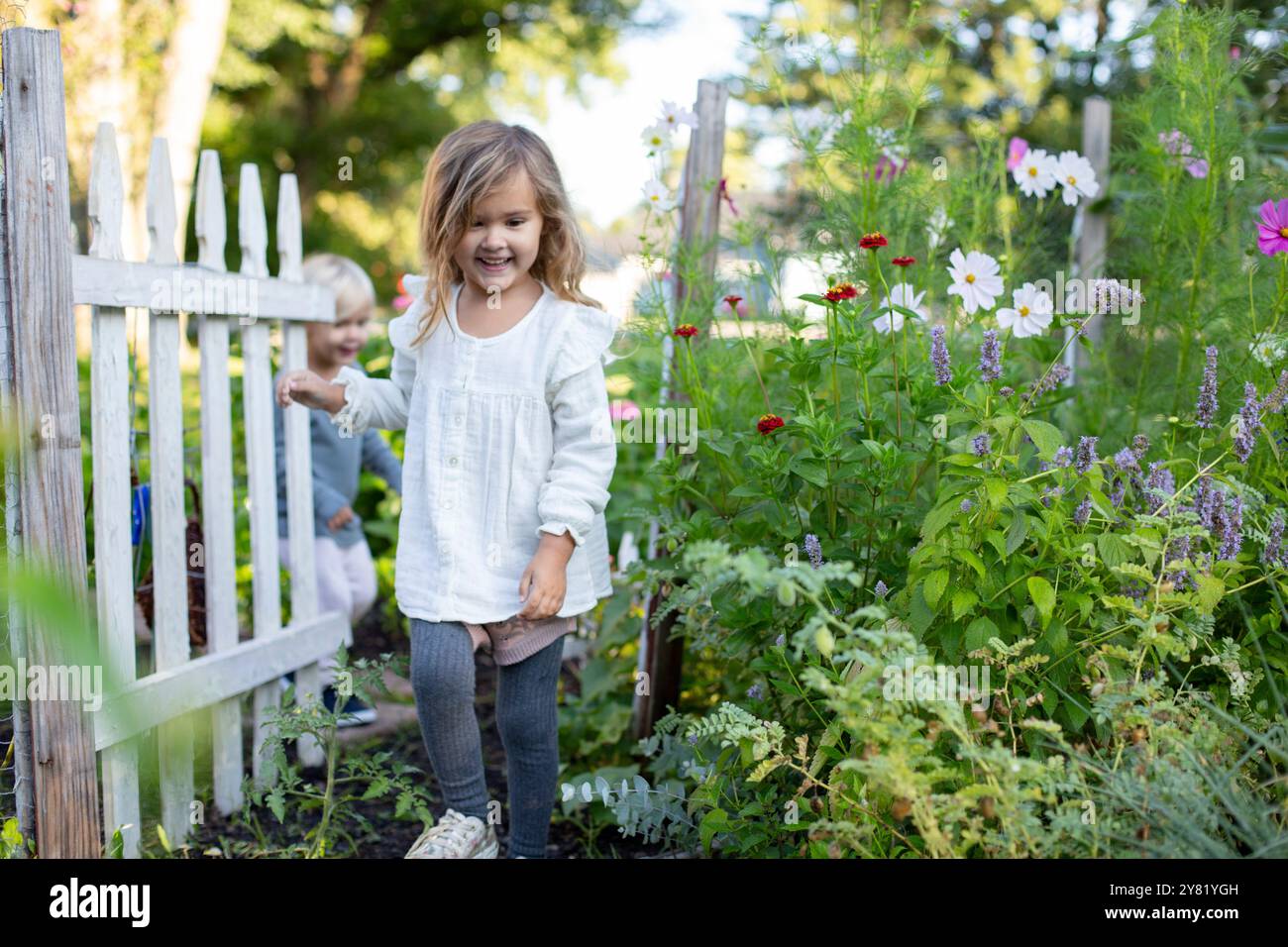 Smiling children playing in a vibrant garden near a white picket fence ...