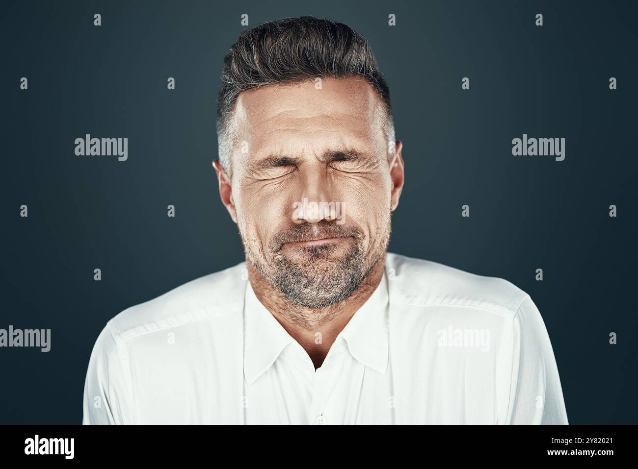 Grimacing. Handsome young man keeping eyes closed and inflating cheeks ...