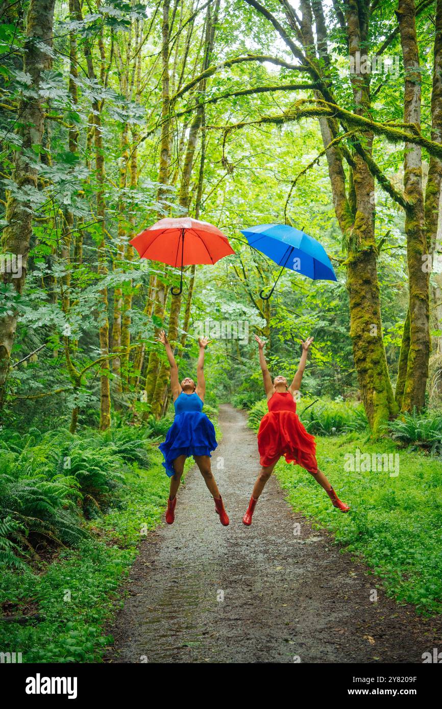 Two people joyfully leap into the air on a forest path, each holding a ...