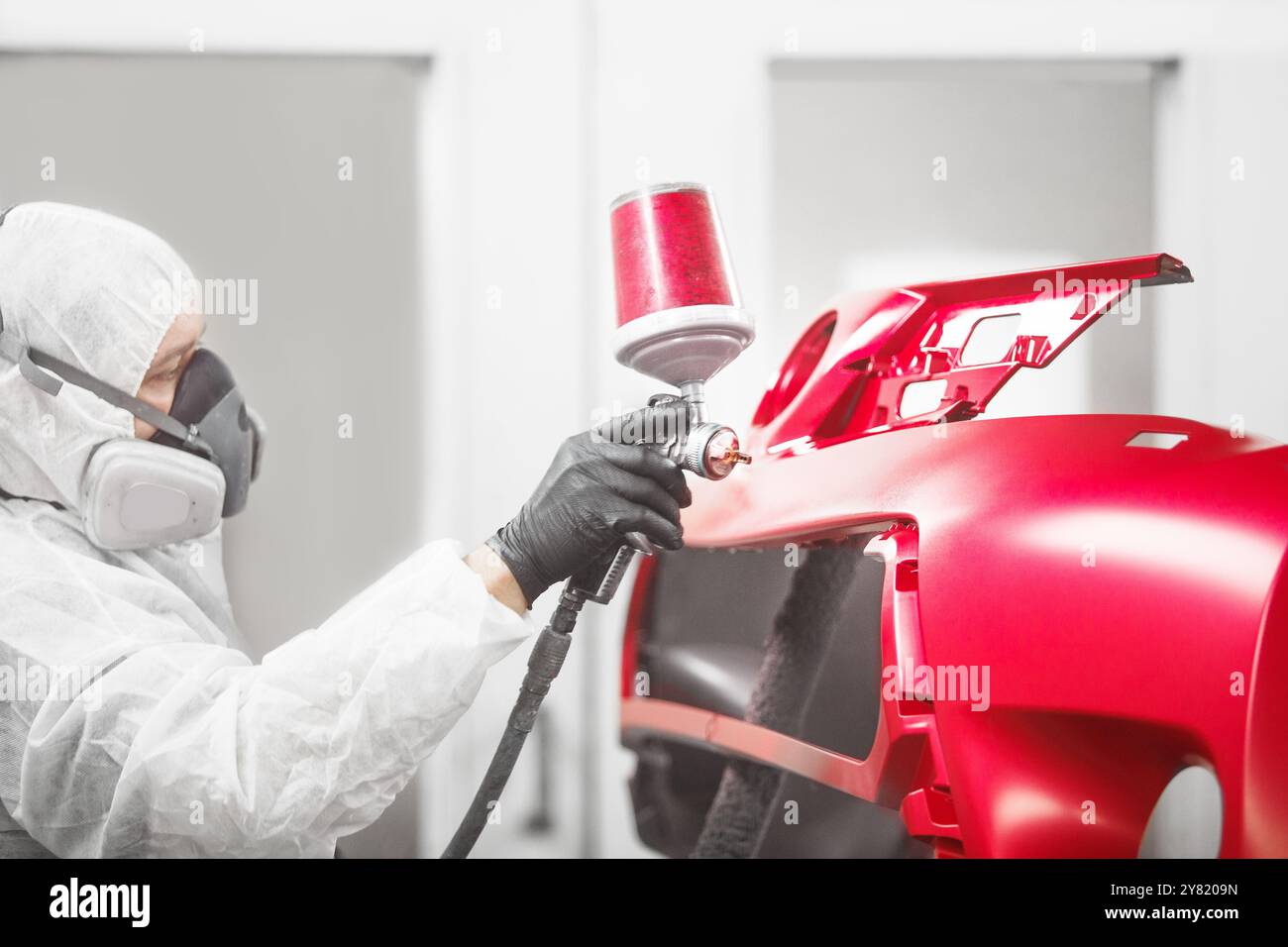 Auto mechanic worker painting car bumper with spray gun in a paint ...