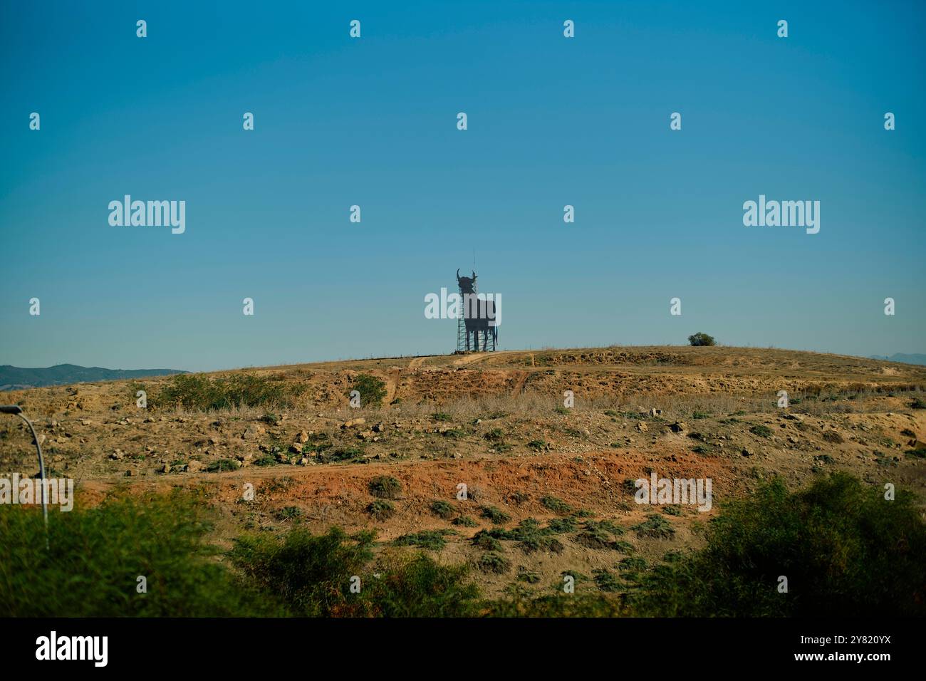 An imposing sculpture of a bull stands atop a hill under the clear blue ...