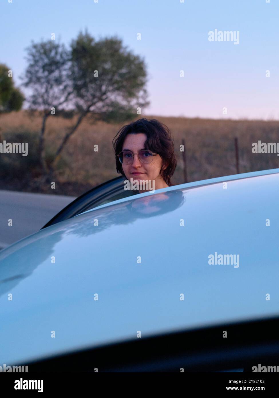 Woman with glasses peeking out from the driver's side of a car with ...