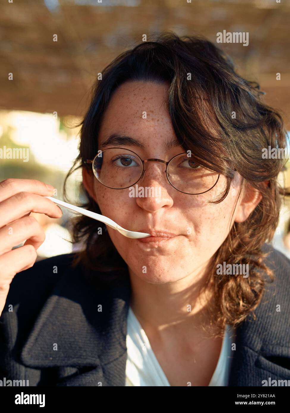 Woman enjoying a spoonful of food outdoors with sunlight illuminating ...