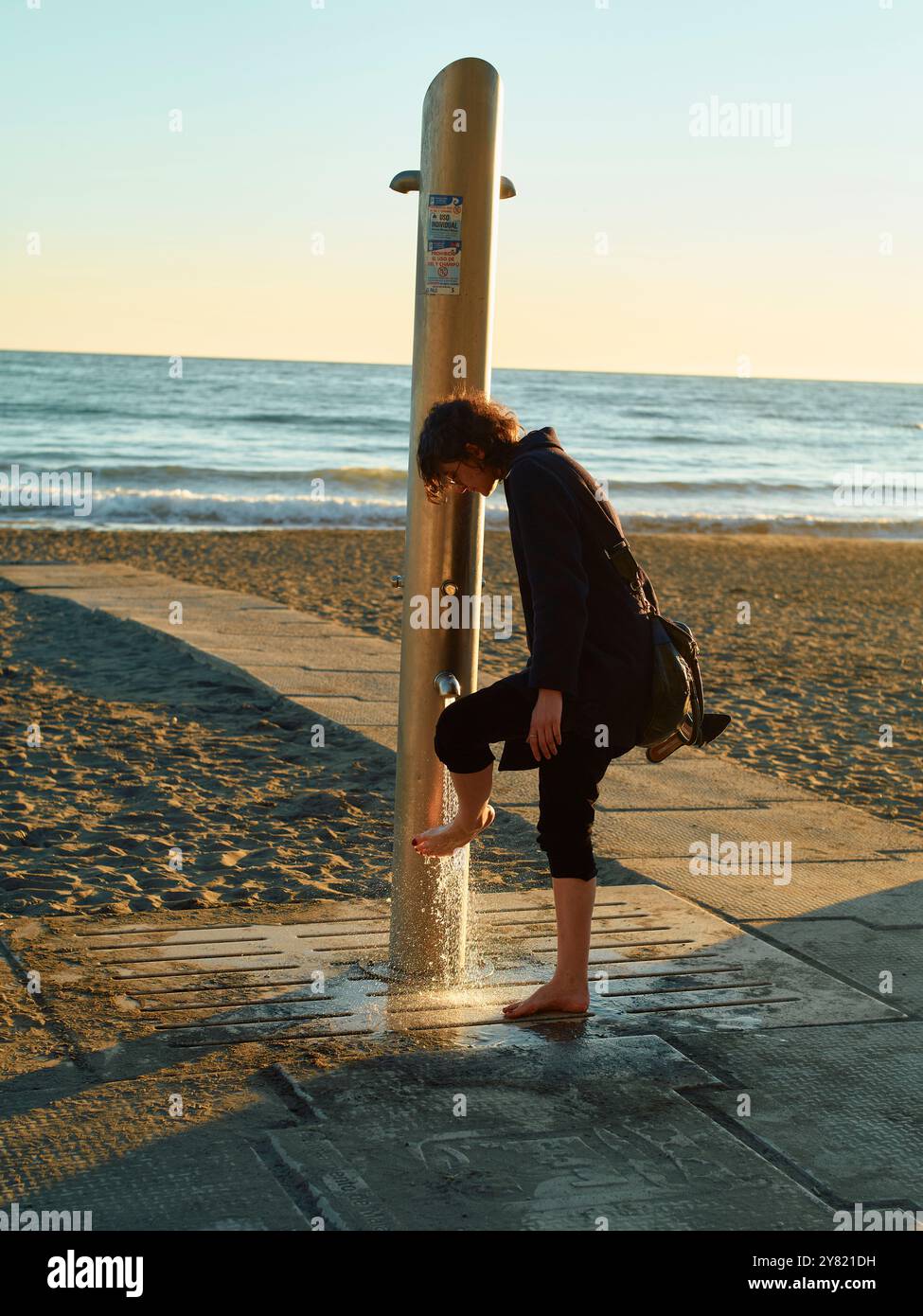 Person rinsing sand off their foot at a beachside shower during sunset ...