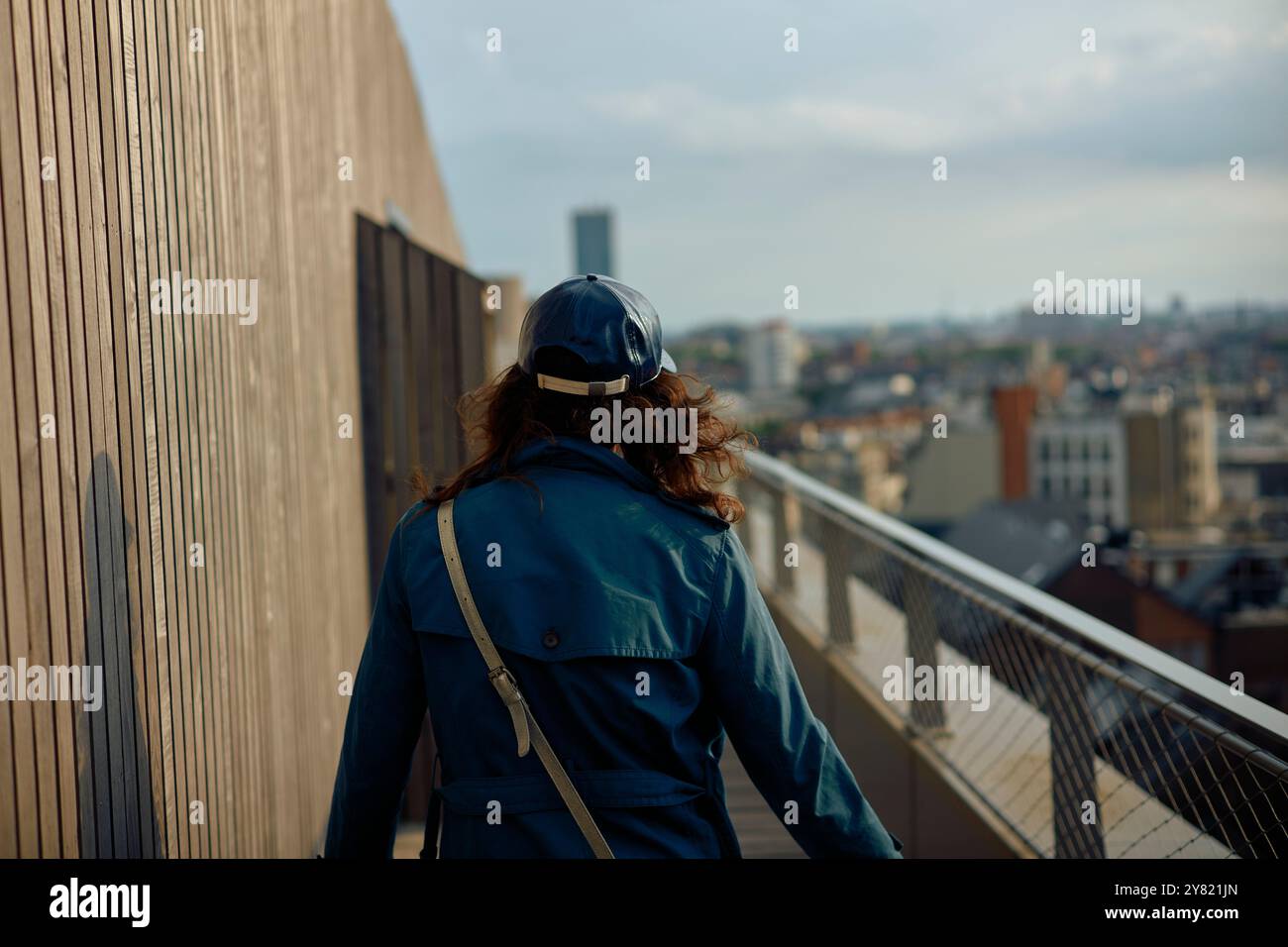 A woman in a blue jacket and backpack walks along an elevated walkway ...