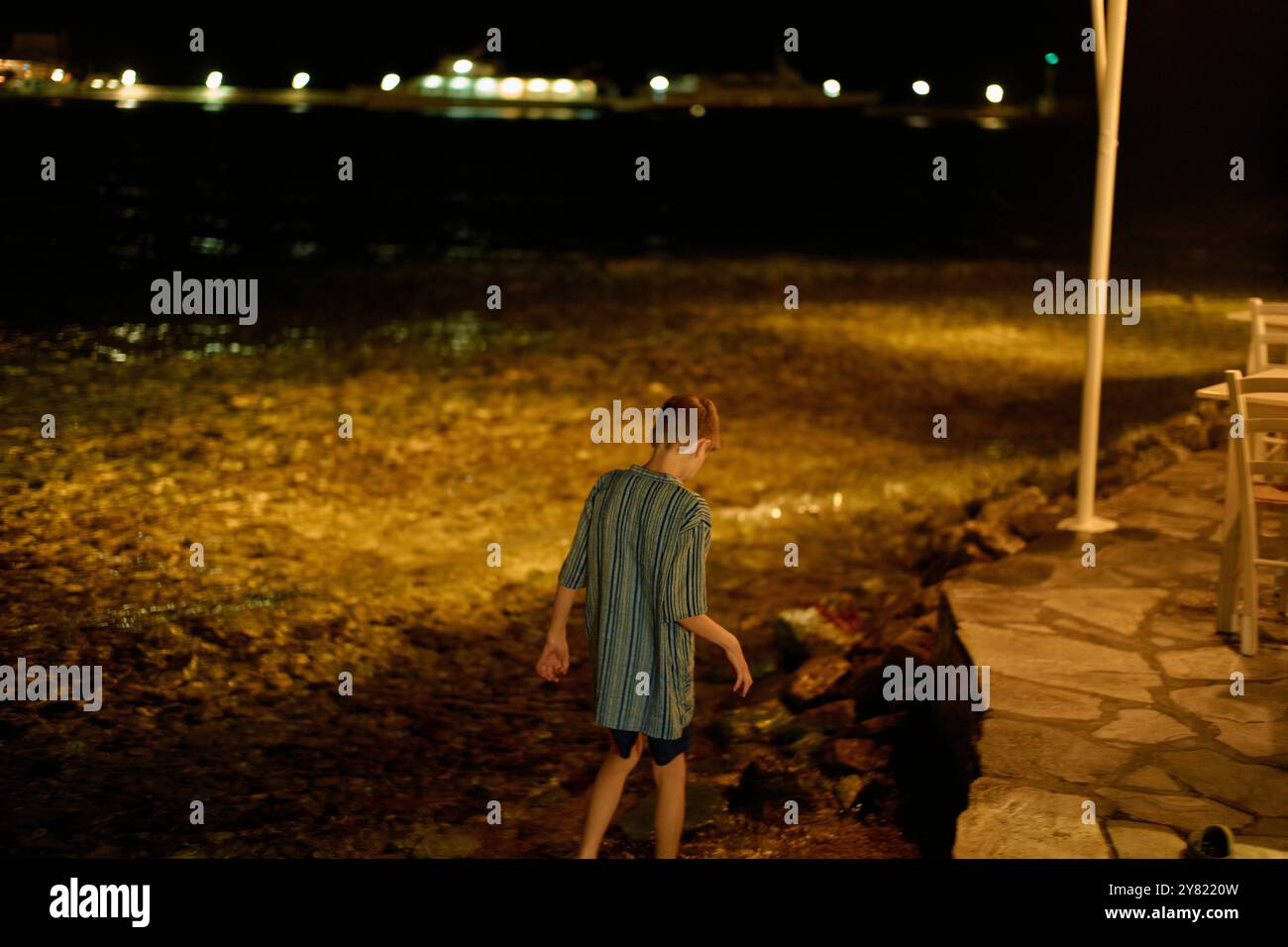 Child in striped clothes walking by a seaside at night under ambient ...