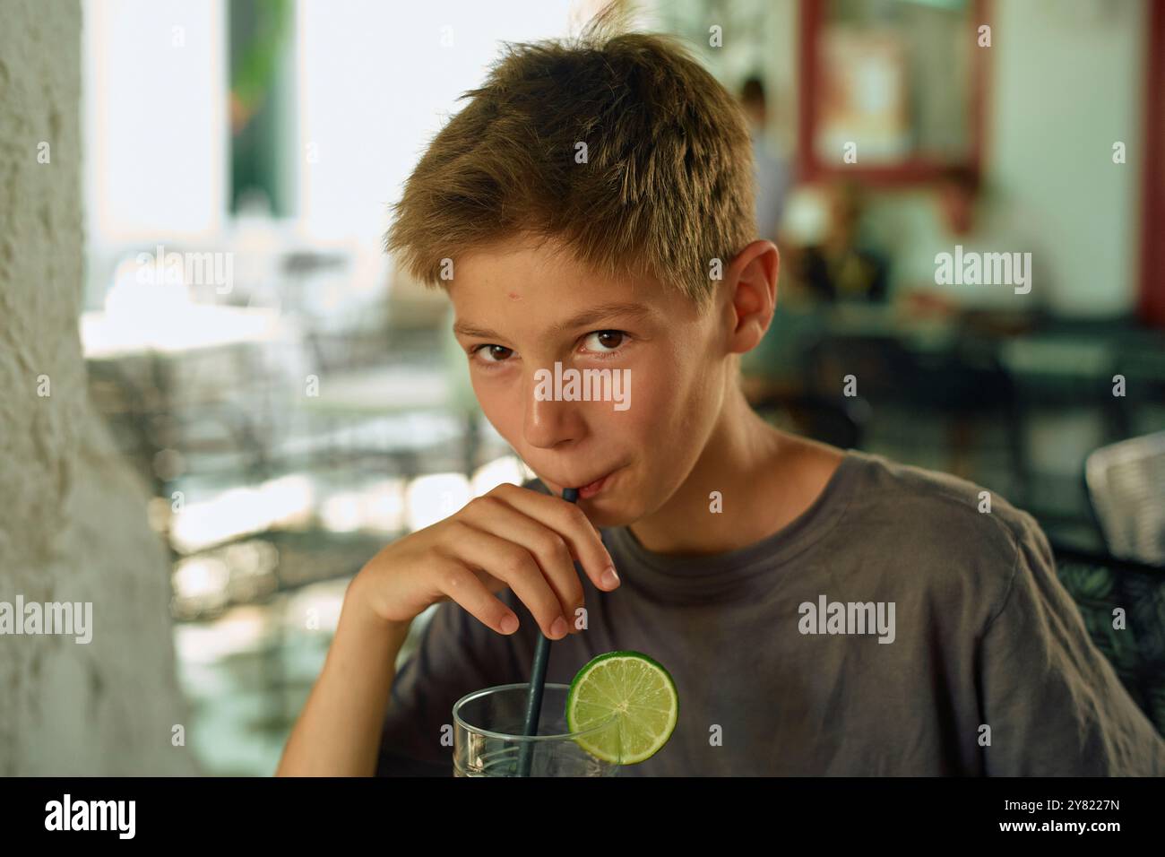 A teenager enjoys a refreshing beverage with a slice of lime, giving a ...