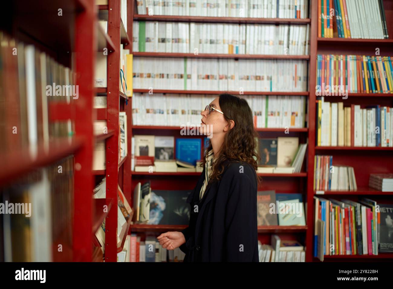 Woman browsing books in a library with red shelves Stock Photo - Alamy