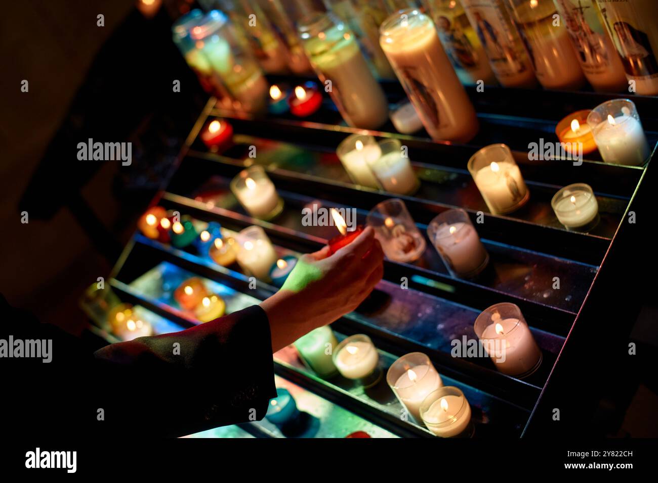 Hand lighting candles on a multi-tiered candle stand in a dimly lit ...