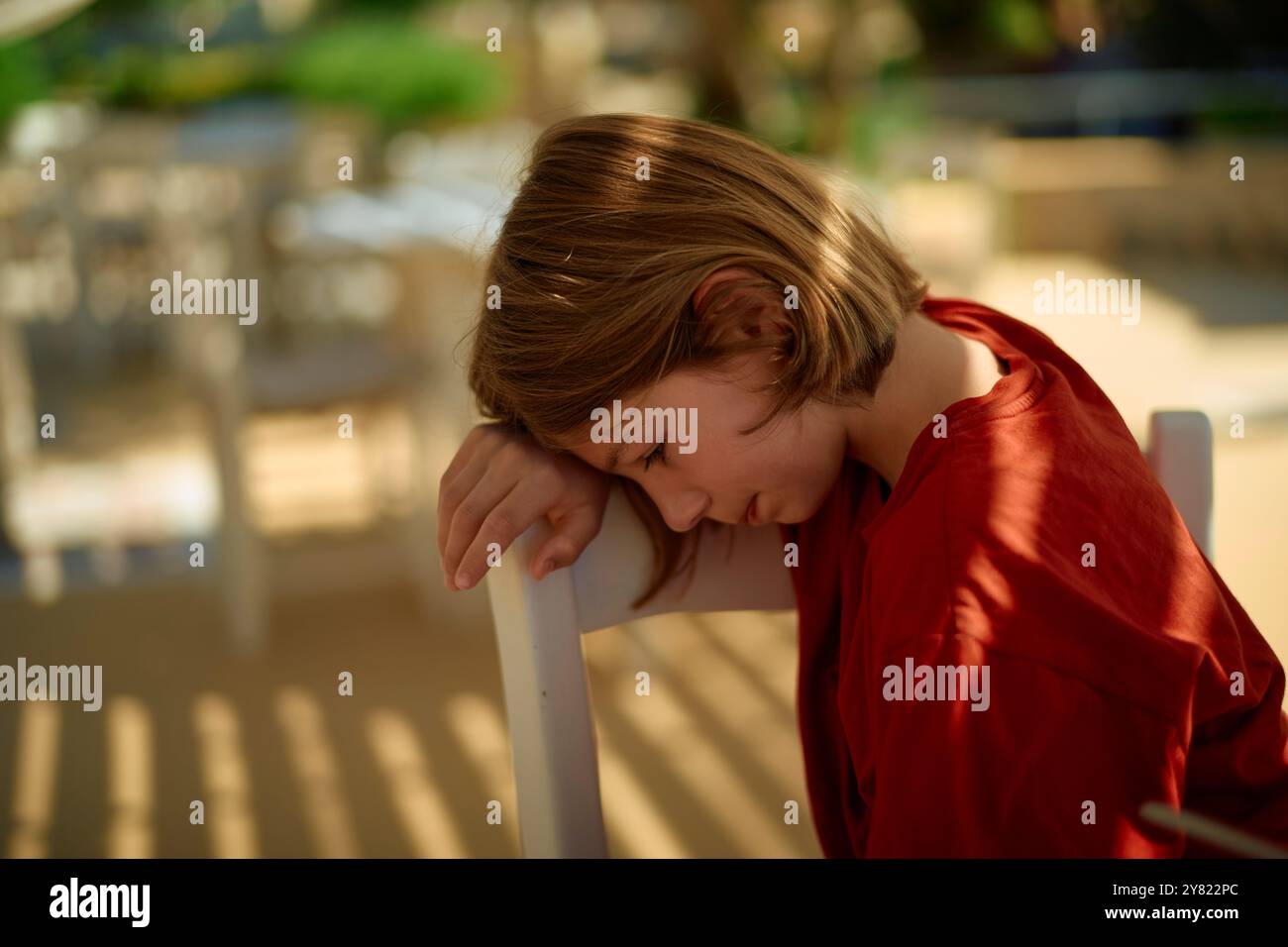 A thoughtful child rests their head on their arm, which is leaning on ...