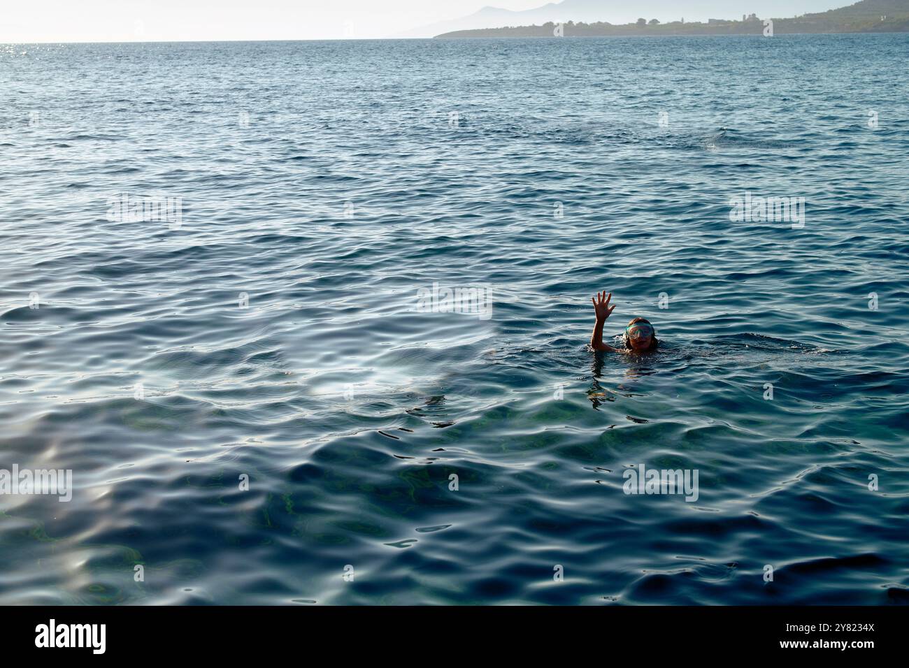 Swimmer signaling for help in the ocean with calm water and a clear sky ...