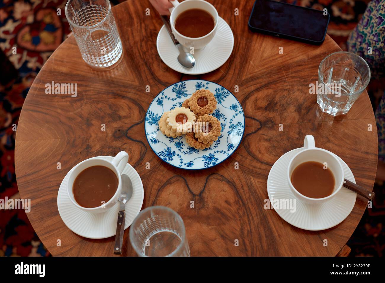 Overhead view of a wooden table with three cups of coffee, a plate of ...
