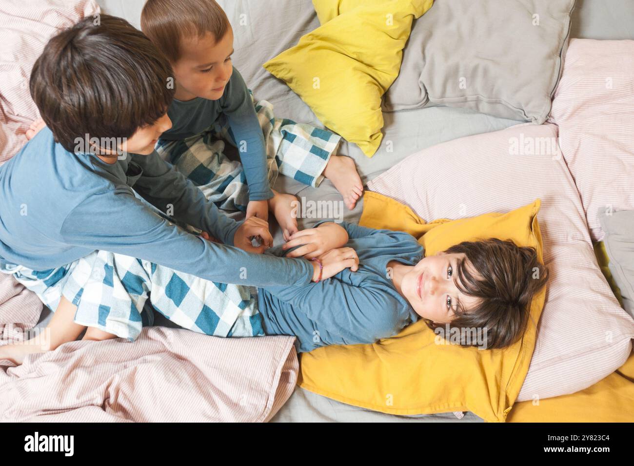 Three children play tickling games on a bed full of pillows. One of ...