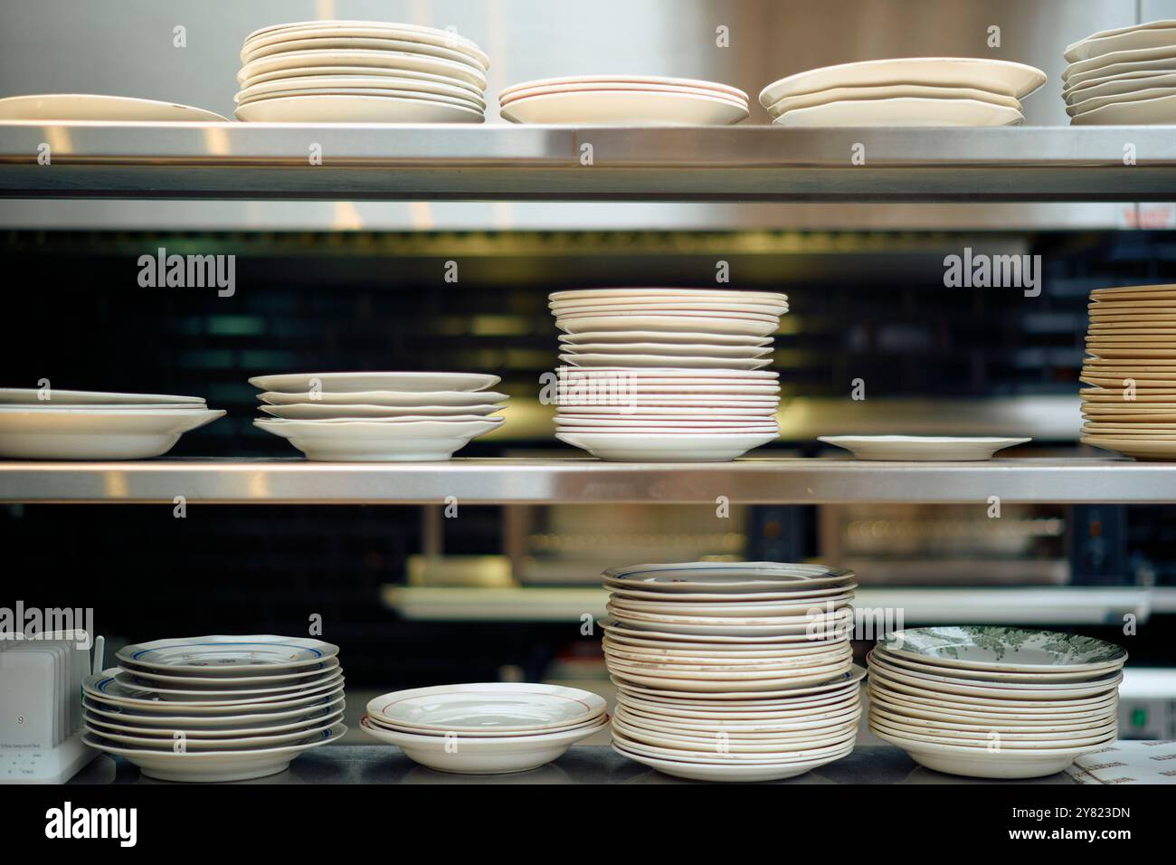 Stacks of various white ceramic plates on metal shelves in a commercial ...