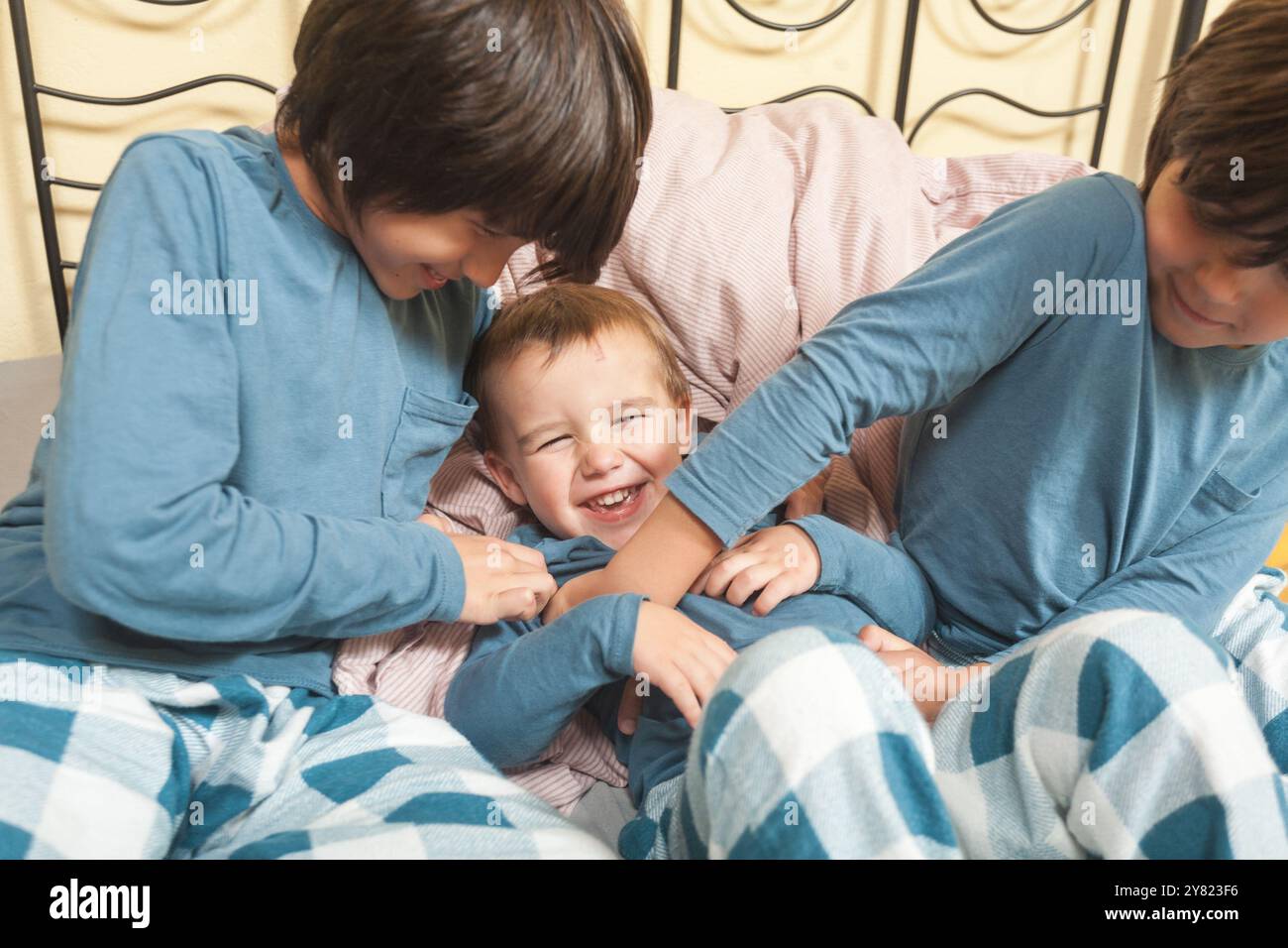 Three boys in the same blue pajamas play together in bed and tickle ...