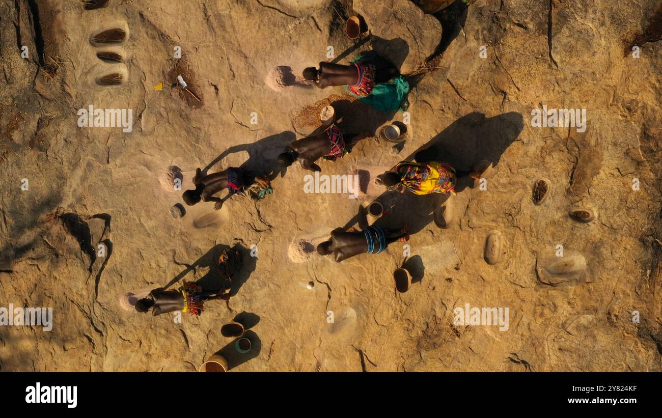Larim tribe women grinding sorghum grains in holes in a rock, Boya ...
