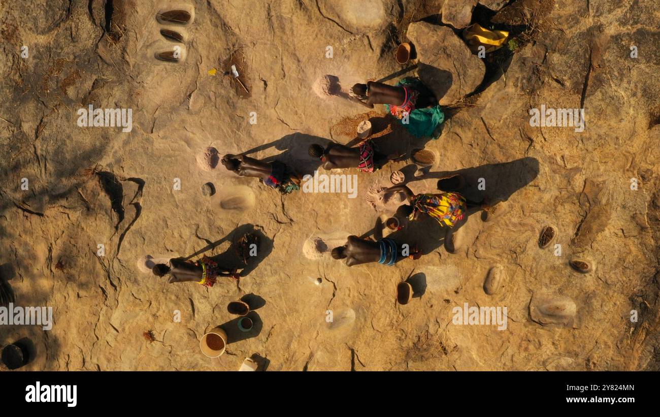 Larim tribe women grinding sorghum grains in holes in a rock, Boya ...