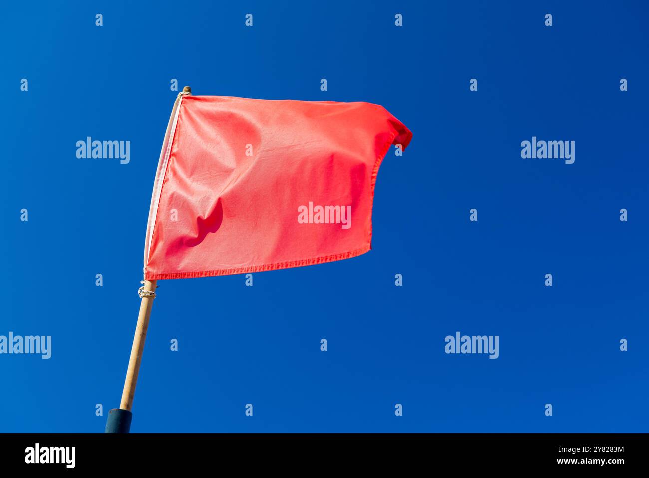 Warning red flag is waving on strong wind above blue sky on the beach ...