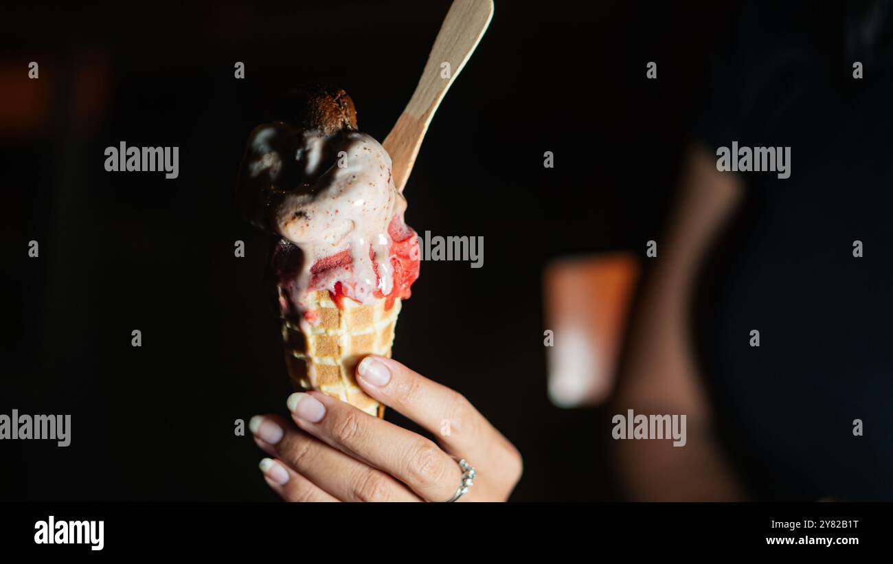 A close-up of a hand holding an ice cream cone with three scoops of ...